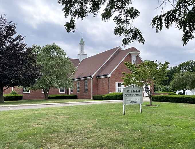 St. George Catholic Church rises quietly against a cloudy sky, its white steeple cutting through the grey like a gentle exclamation point.