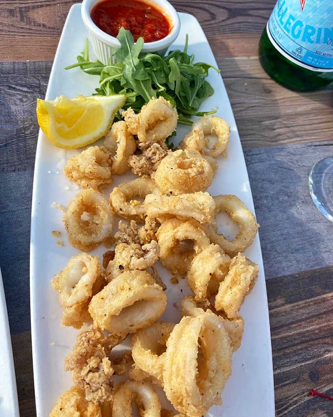 A long platter of crispy calamari rings with marinara and lemon, San Pellegrino standing by. Italy would approve completely.