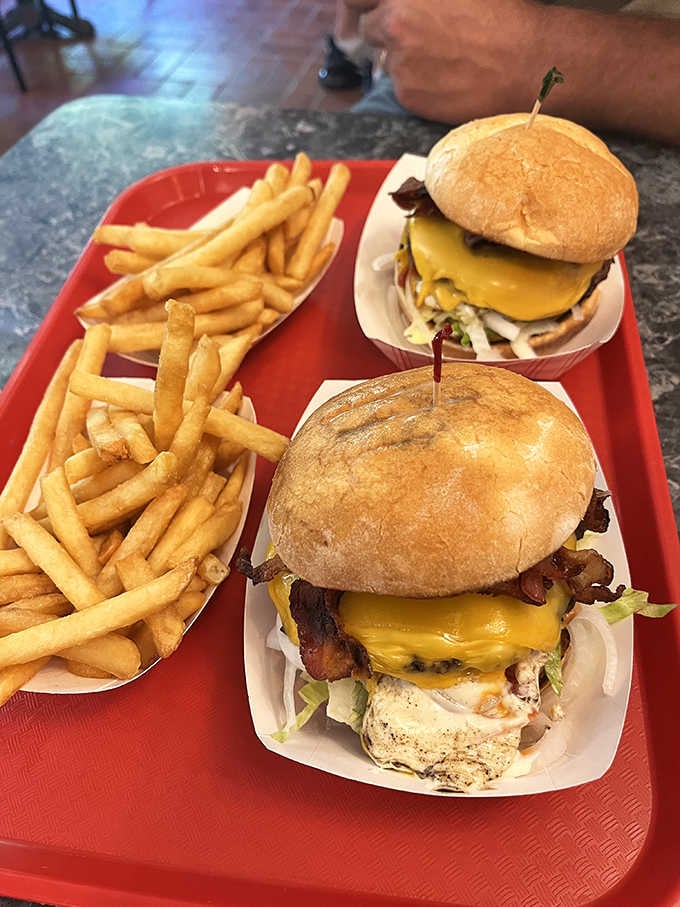 Dig into two juicy bacon cheeseburgers loaded with toppings, perfectly paired with golden, crispy french fries on a red tray.