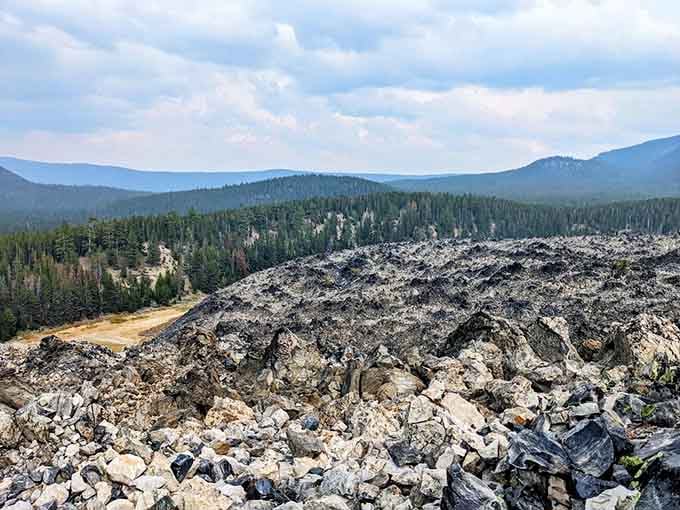 The Big Obsidian Flow up close, all jagged black glass and raw geological drama stretching toward distant mountains.