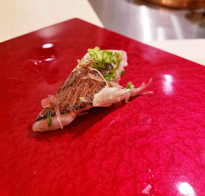Scored mackerel resting on crimson lacquer, topped with scallion and bonito flakes, is a bite that knows exactly what it's doing.