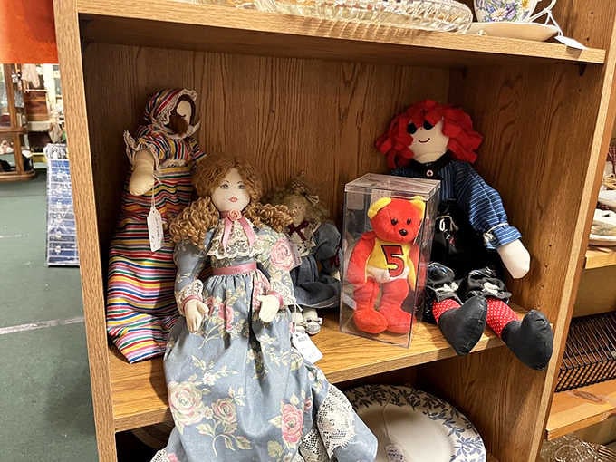 Fabric dolls, a boxed collectible bear, and a red-haired rag doll sharing a shelf like old friends reunited at last.