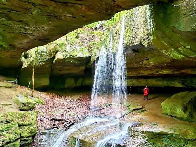 One visitor in red stands small beneath a thundering curtain of water, a reminder that nature always wins the size comparison.