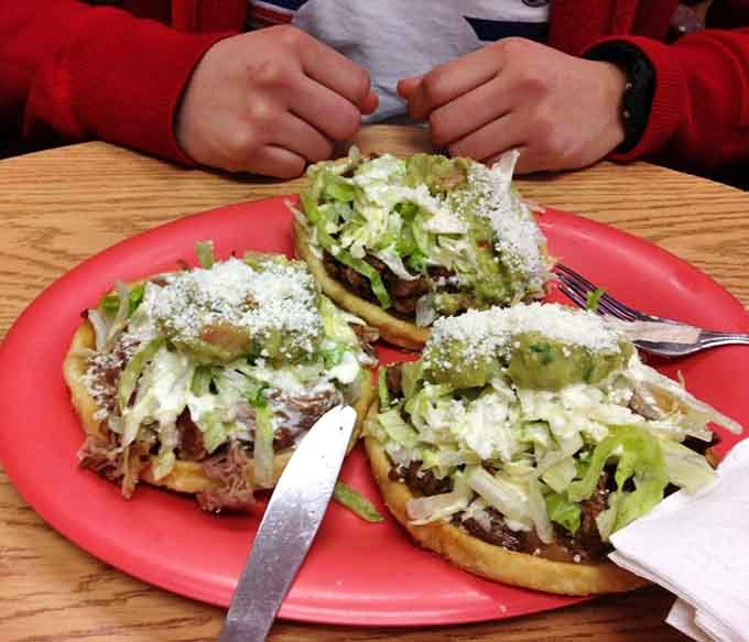 Sopes loaded with shredded meat, lettuce, guacamole, and crumbled cheese on a bright red plate. Pure, unapologetic comfort food at its finest.