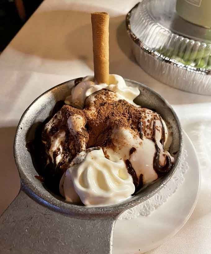 Holly's Adobe Sundae arrives in a tin bowl with chocolate drizzle and a wafer. Dessert with genuine frontier charm.