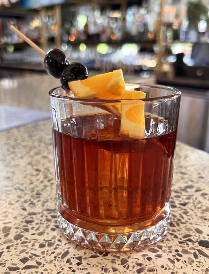 An old fashioned garnished with cherries and orange peel, sitting at the bar like it belongs in a movie.