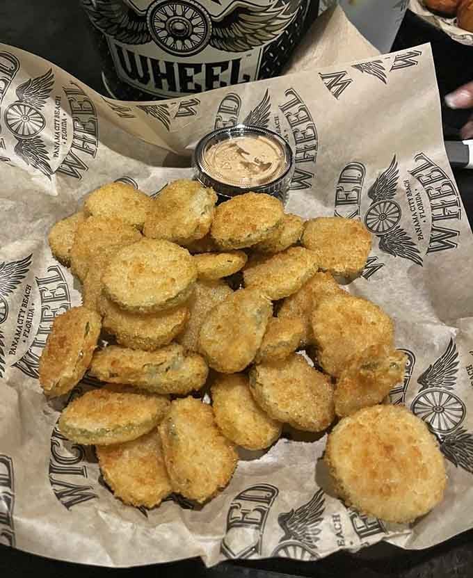 A mountain of fried pickle chips served on branded Wicked Wheel paper, crispy, tangy, and completely impossible to stop eating.