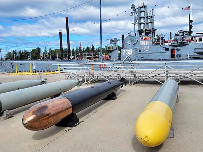 Torpedoes lined up dockside with hull 236 standing watch behind them, a quiet reminder of what this vessel was built to do.