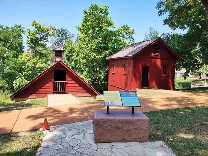 Two bold red outbuildings standing under a canopy of trees, each one carrying a chapter of this property's layered working history.