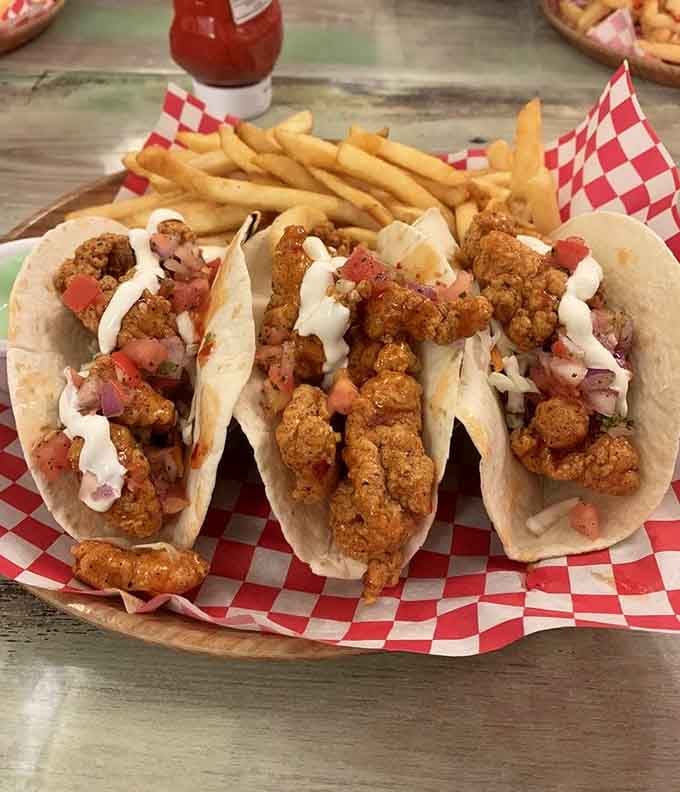 Three alligator tacos piled high with crispy bites, fresh pico, and cream, flanked by golden fries ready for action.