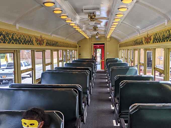 Rows of classic seats, warm ceiling lights, and decorative trim, this coach interior is giving full golden-era railroad elegance.