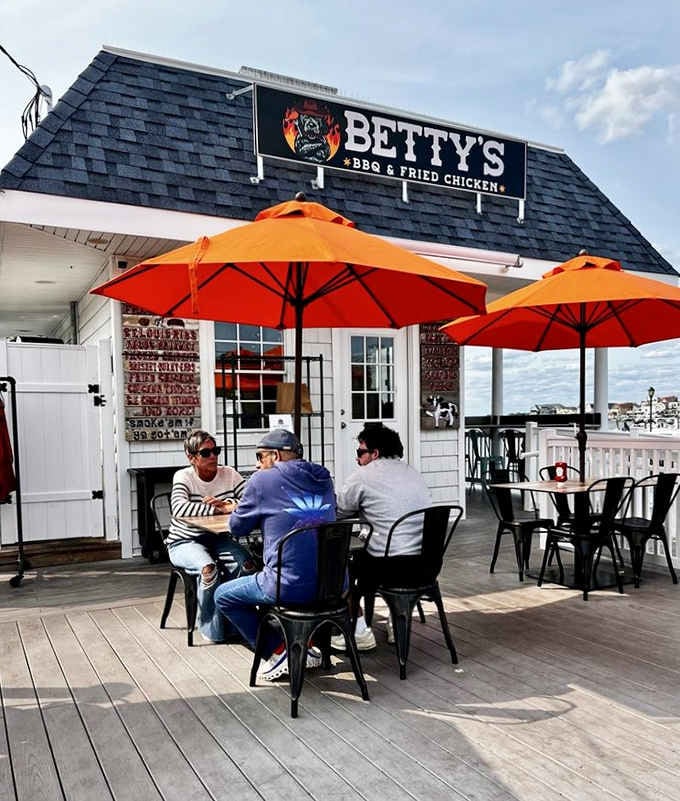 Bold orange umbrellas pop against the white deck railing as a group of friends settles in for a perfect seaside meal.