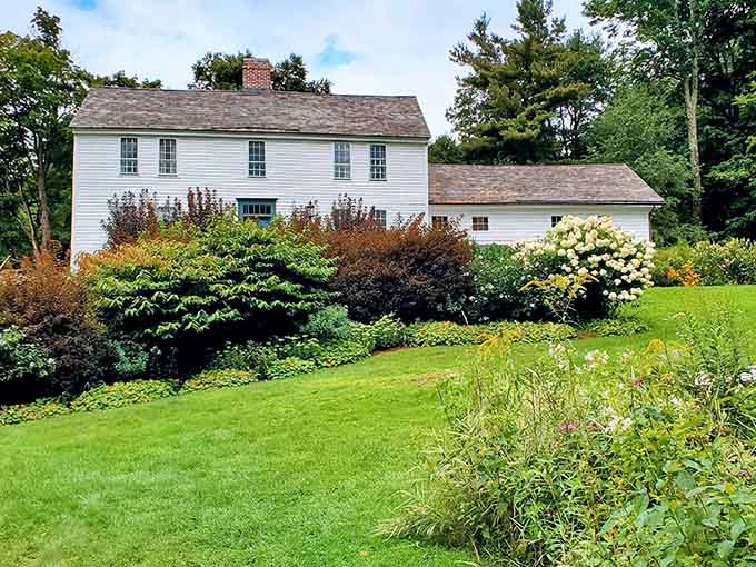 Lush landscaping frames the historic white clapboard home, where centuries-old architecture meets carefully tended modern gardens beautifully.