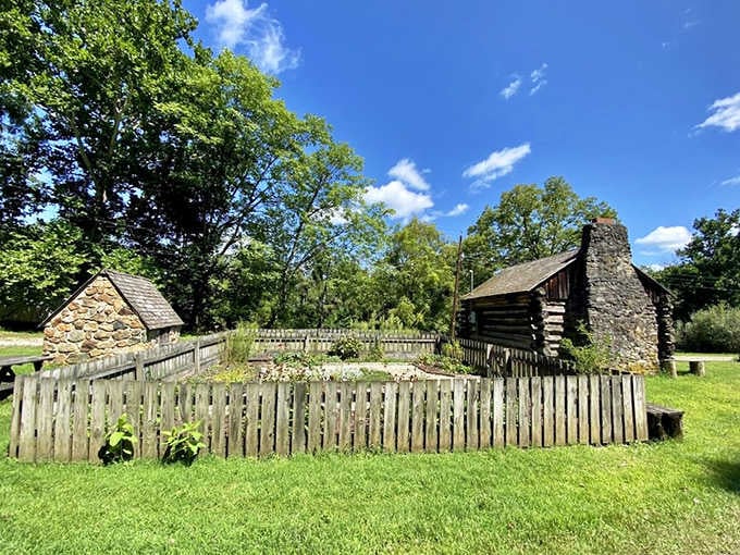 A log cabin and stone springhouse stand behind a weathered fence, quietly telling stories that no history book could fully capture.