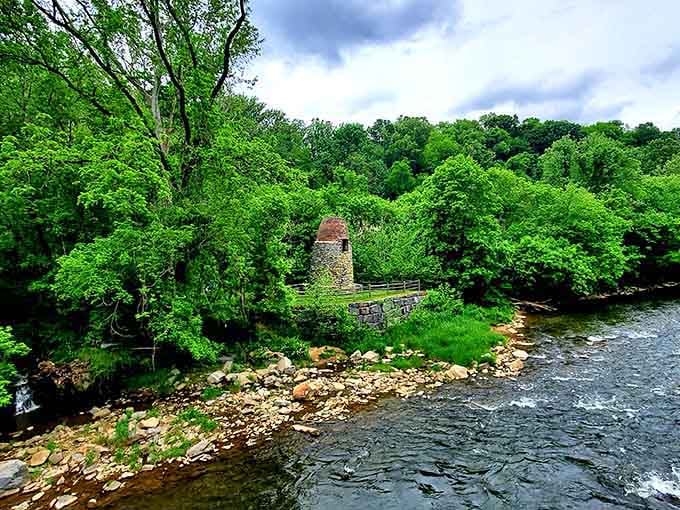 A centuries-old stone mill tower peeks through an explosion of lush green foliage beside the rushing river, looking wonderfully stubborn and timeless.