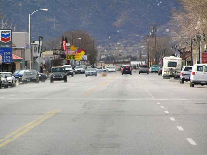 A wide Tehachapi boulevard stretches toward mountain foothills, with a roadside cafe sign promising something warm and satisfying ahead.