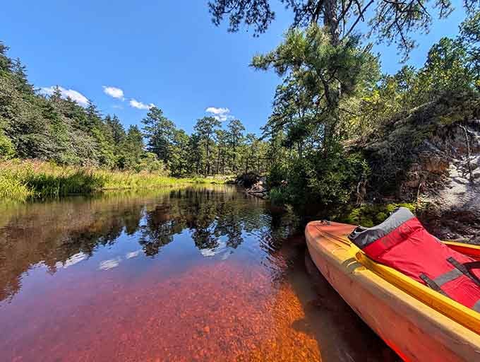 A kayak rests beside tea-colored water that reflects the pines, ready for your own Huckleberry Finn adventure.