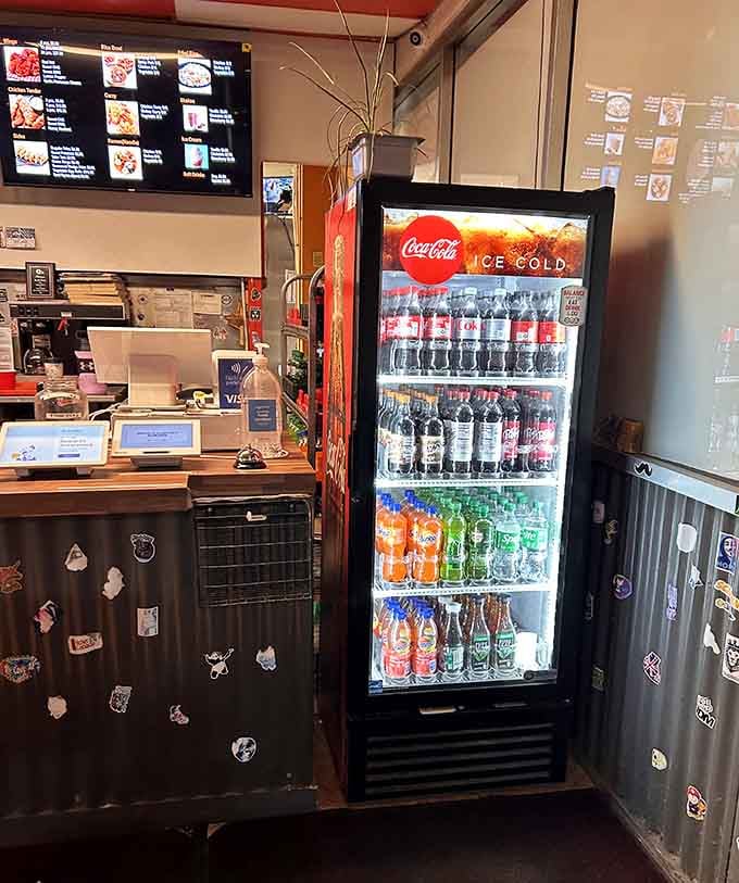 A glowing Coca-Cola cooler, a service counter covered in stickers, and digital menus overhead. This ordering station has genuine personality baked right into it.