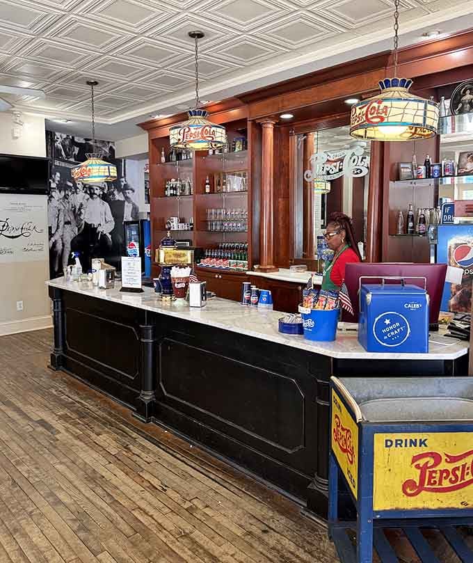 A marble-topped soda counter, warm wood columns, and stained glass Pepsi lamps overhead. This room earns its history.