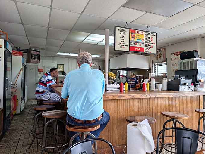 Round wooden stools pulled up to a warm counter. This is where regulars sit, eat, and solve the world's problems over chili dogs.