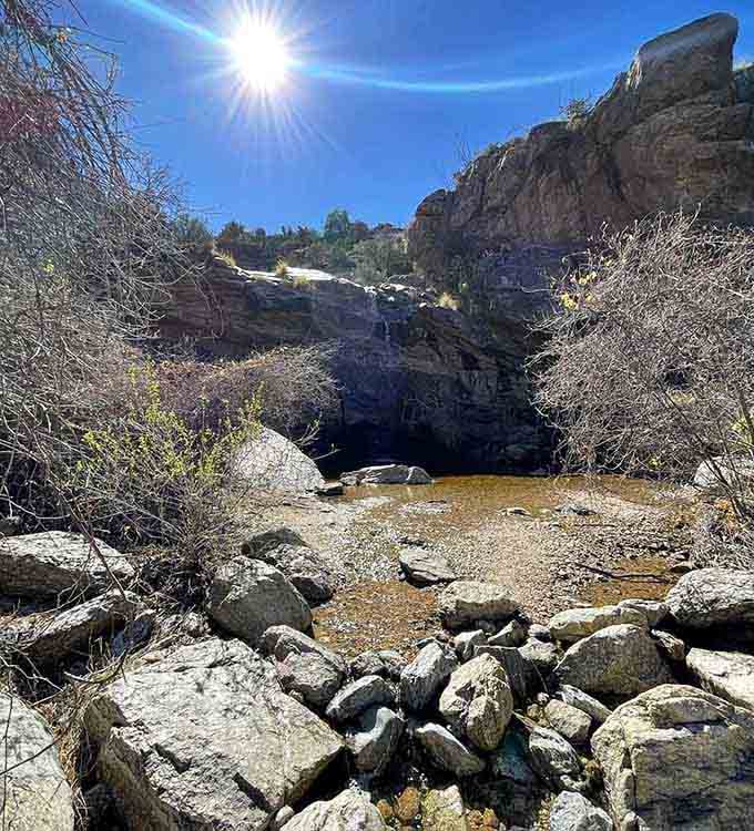 Sun-drenched rocks frame the shadowy grotto where cool water waits to reward hikers who made the desert trek worthwhile.