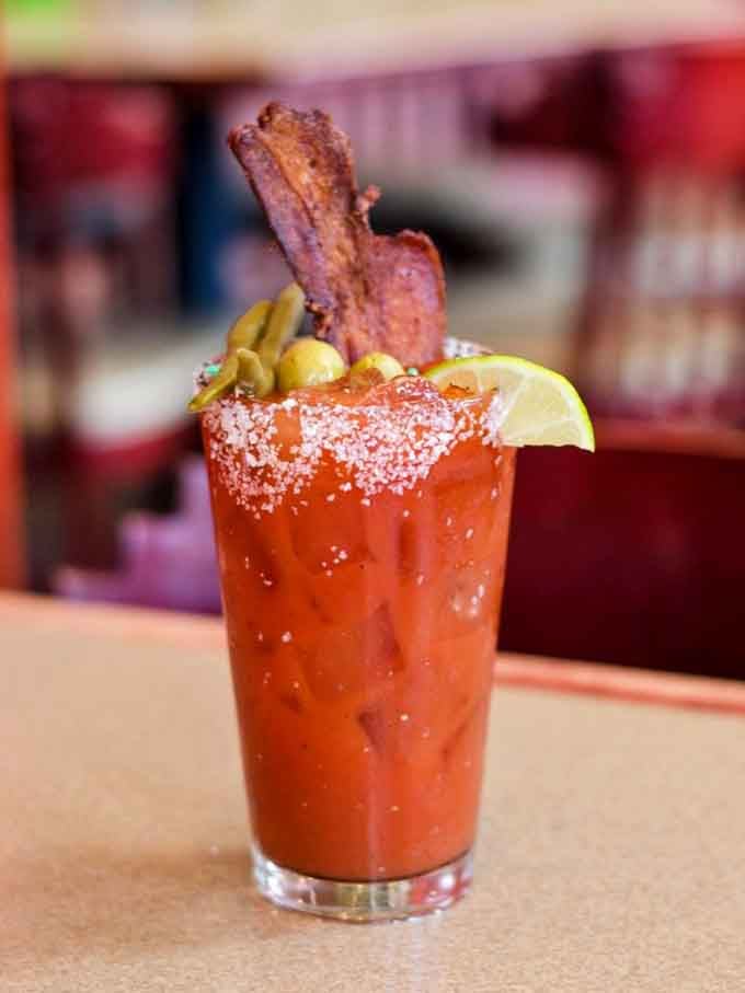 A Bloody Mary garnished with bacon standing tall like a delicious flag of weekend victory and good decisions.