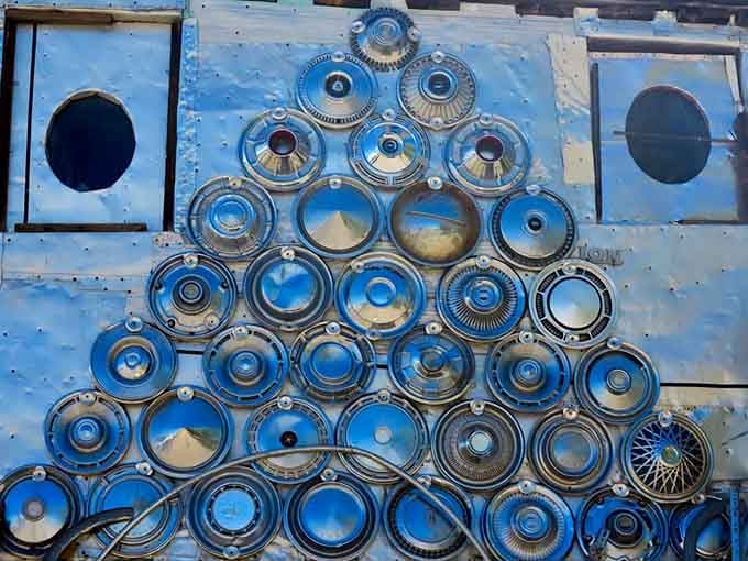 A wall of hubcaps arranged in a gleaming triangle pattern, reflecting the Colorado sky back at you like a funhouse mirror.