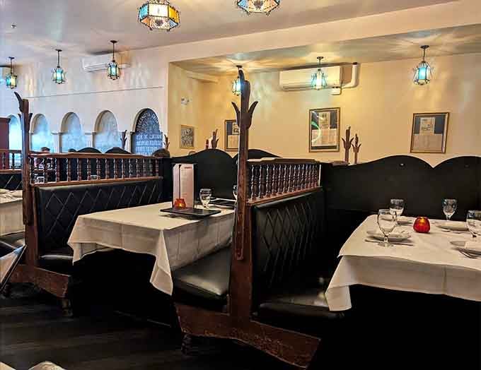 White tablecloths, tall dark booths, arched details on the walls, and stained-glass light overhead. This room has been perfected over a very long time.
