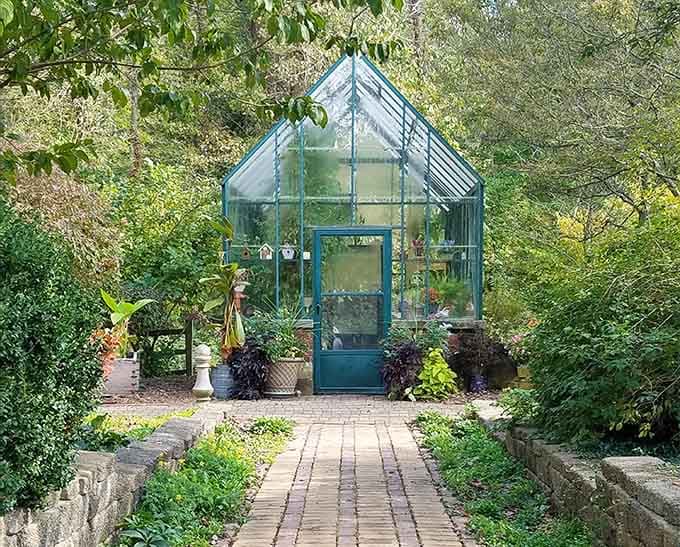 A teal greenhouse tucked among the trees, quietly growing things and minding its own beautiful business.
