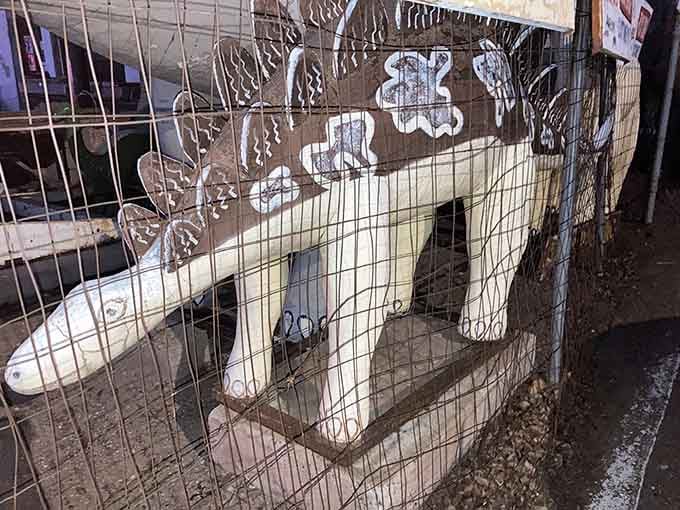 A painted stegosaurus tucked behind the fence, quietly waiting for someone to finally notice it.