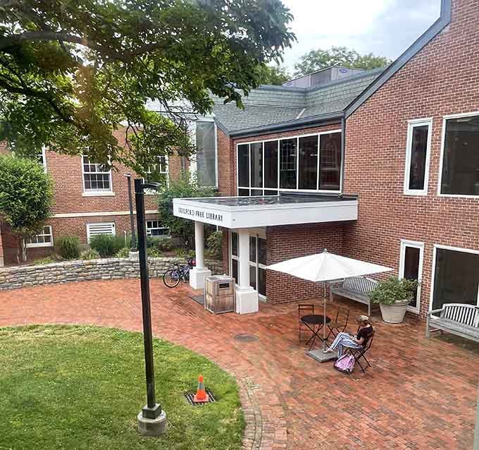 Someone found the best seat at the Guilford Free Library's brick courtyard, and honestly, that umbrella table setup is goals.