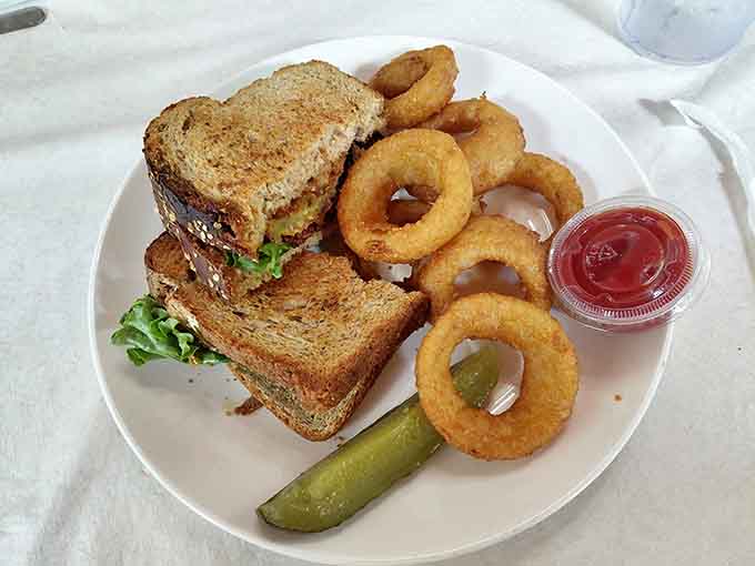 A toasted sandwich with crispy onion rings and a pickle, proof that the classics never need reinventing.