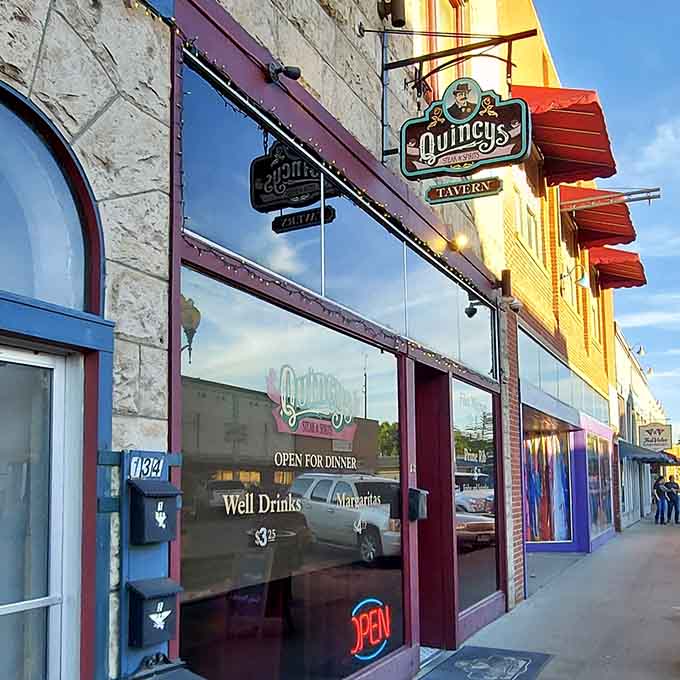 Quincy's Tavern sign swings above a glowing neon OPEN sign, promising steaks, spirits, and the kind of evening you'll be talking about tomorrow.