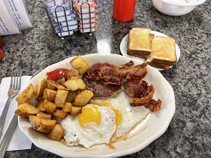 Two sunny side up eggs, crispy bacon, a sausage patty, homefries, and toast on the side. A full breakfast plate that delivers on every promise.