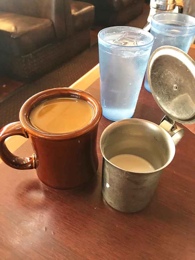 A warm ceramic mug of coffee beside a classic metal creamer pot. Simple, honest, and exactly what mornings were made for.