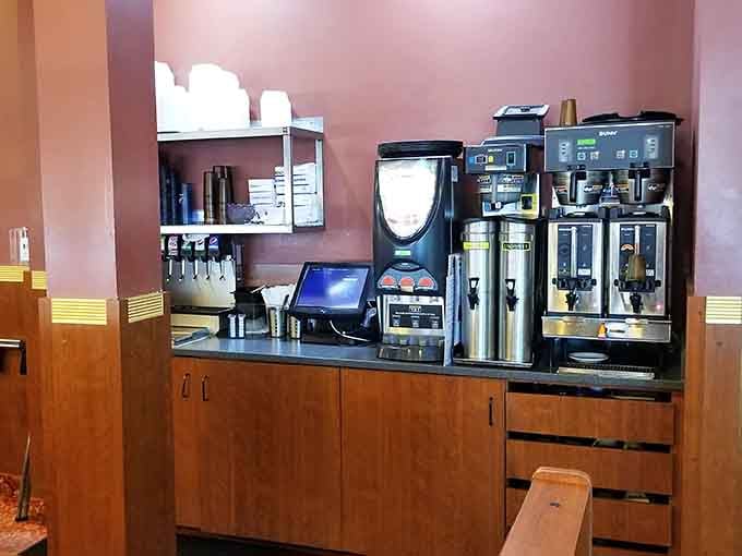 The coffee station stands ready like a reliable old friend, multiple brewers humming quietly and cups stacked high above.