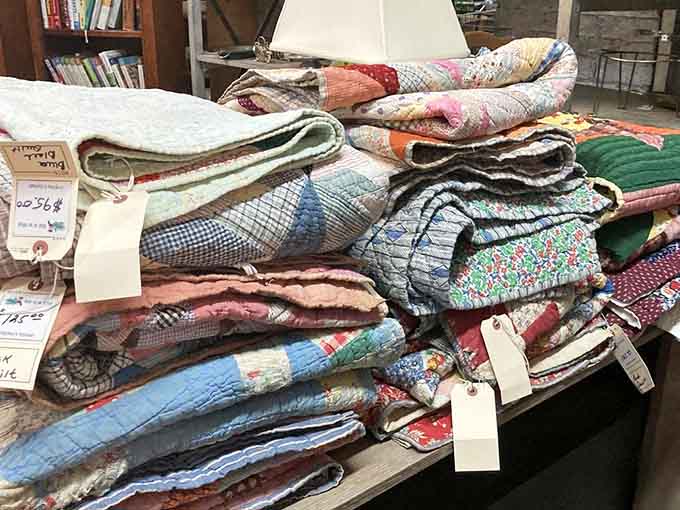 Handmade quilts stack in colorful layers, each one representing hours of someone's loving handiwork.