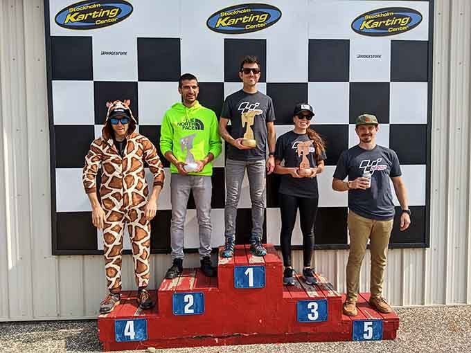 A giraffe on the podium holding a trophy is exactly the kind of energy every race day deserves, honestly.