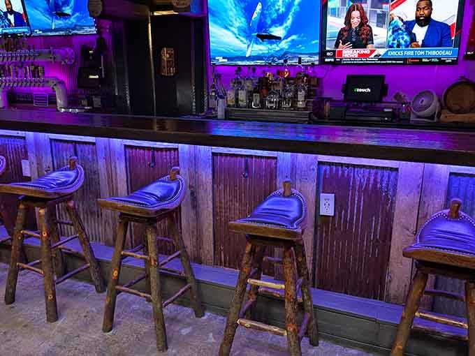 Rustic bar stools belly up to weathered wood paneling, illuminated by that signature purple glow of nighttime ambiance.
