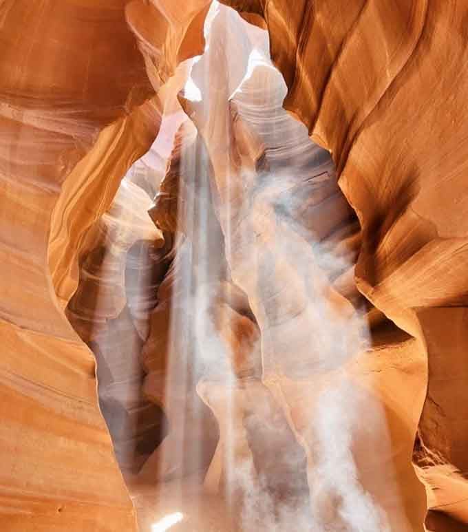A slot canyon frames a beam of light and falling sand, nature putting on its finest show.