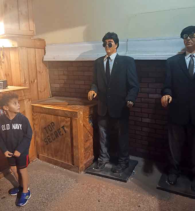 Two very serious Men in Black figures standing guard, and somehow the wooden crate labeled "Top Secret" makes perfect sense.