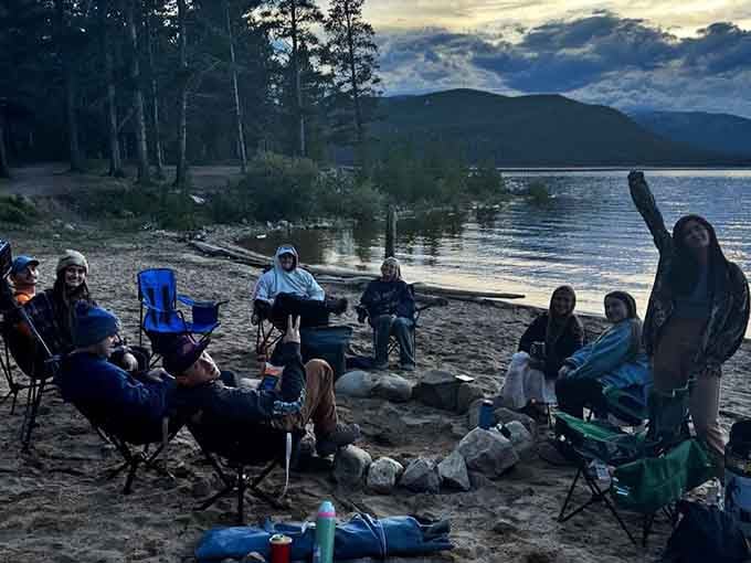 A circle of friends around a lakeshore fire at dusk, proof that the best stories happen right here outdoors.