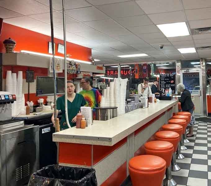 A classic soda fountain counter with orange stools, where every seat comes with a side of good energy.