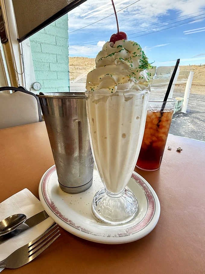 A vanilla shake crowned with whipped cream and a cherry, the Mojave Desert visible right through the window.
