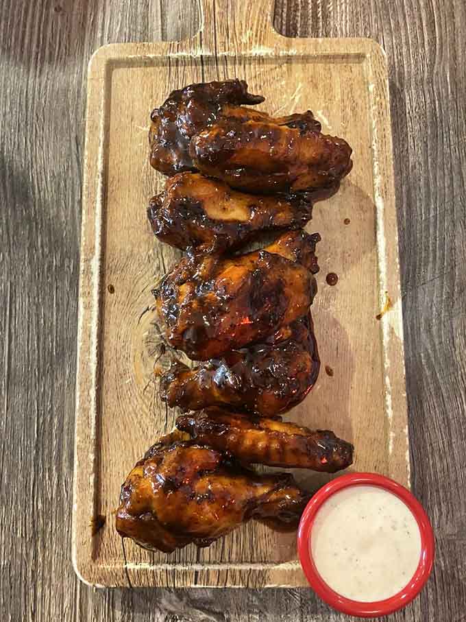 Lacquered, deeply caramelized wings lined up on a wooden board with dipping sauce is a sight that demands your full attention.