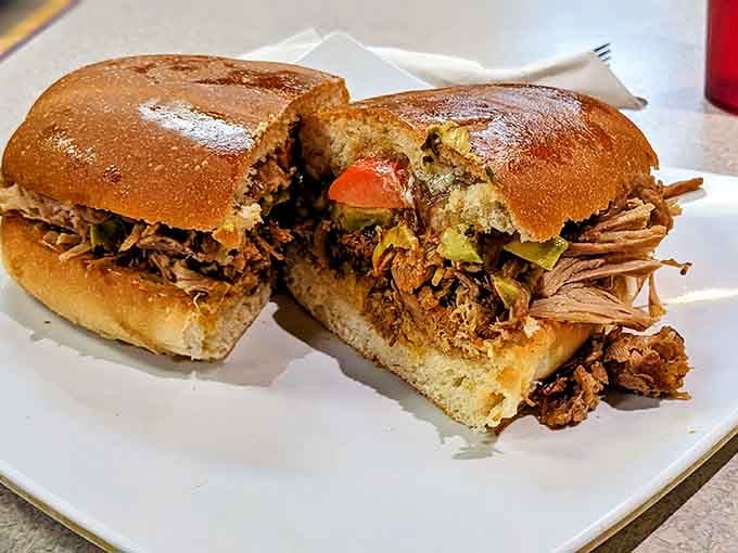 A torta de carnitas cut in half reveals tender, juicy pulled pork tucked into a perfectly golden bolillo.