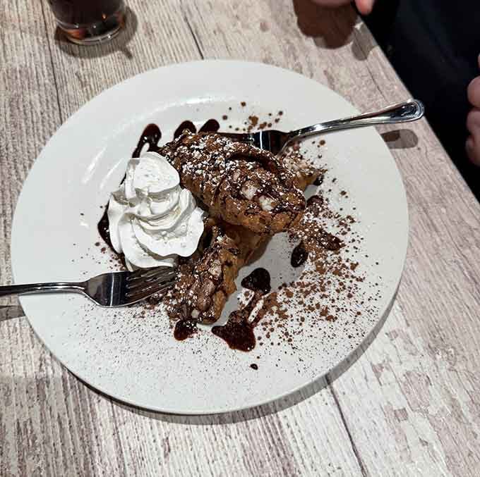 A cannoli dusted with cocoa powder and chocolate drizzle, sitting next to whipped cream like it owns the dessert menu.