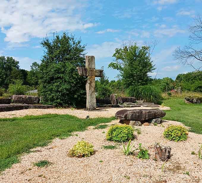 A stone cross rises quietly from the gravel, adding a contemplative, almost cathedral-like stillness to the grounds.