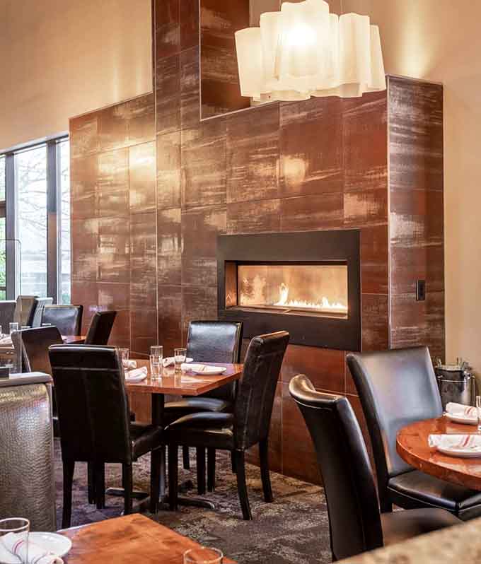 A sleek fireplace set into a rich copper-toned wall with pendant lighting above. Dinner just got considerably more romantic.