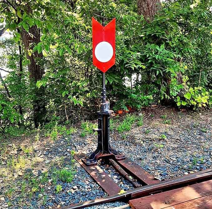 A bright red track switch stand standing guard in the greenery, doing important work and looking sharp doing it.
